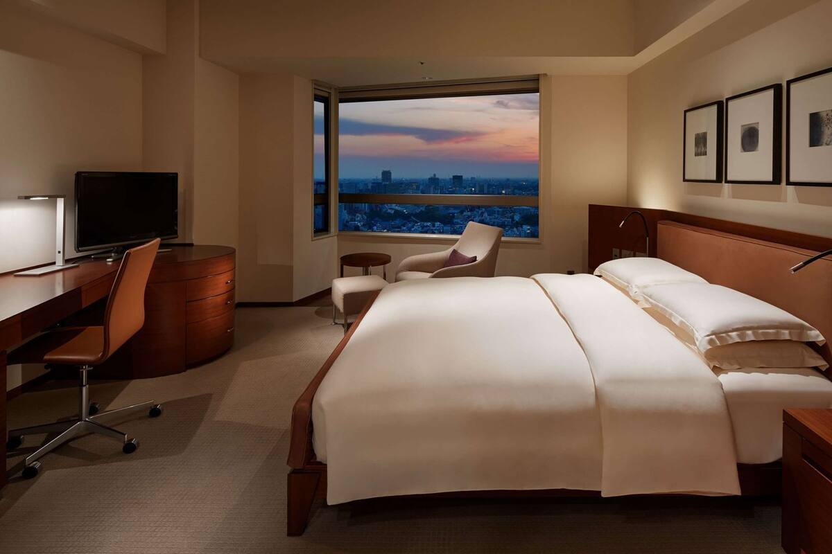 Quarto de hotel com escrivaninha, cadeira, cama e uma grande janela com vista para a cidade.