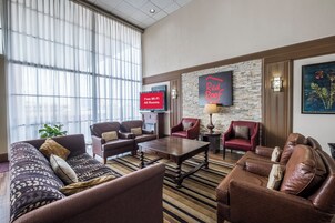 Um saguão de hotel com sofás de couro, uma mesa de centro e uma televisão exibindo 'Wi-Fi Gratuito em Todas as Quartas', e uma placa com a inscrição 'Red Roof Inn'.