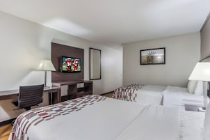 Quarto de hotel com duas camas, uma escrivaninha, uma cadeira, uma televisão e um espelho.
