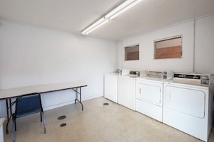 Uma lavanderia com mesa, cadeiras e várias máquinas de lavar roupa.