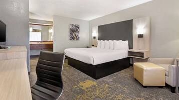 Quarto de hotel com cama, escrivaninha, cadeira, mesa pequena e sofá.