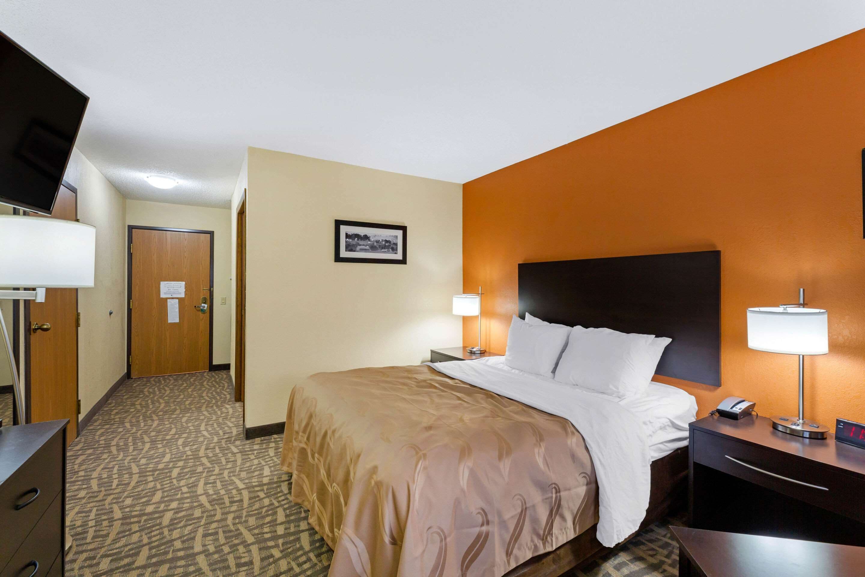 Quarto de hotel com cama, mesas de cabeceira, televisão e um quadro pendurado na parede.