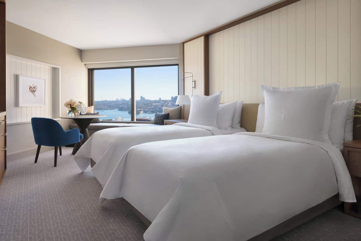Quarto de hotel com duas camas, uma escrivaninha e vista para a cidade.