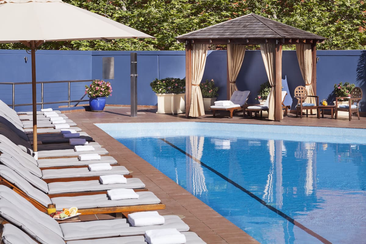 Área de piscina com espreguiçadeiras, um gazebo e plantas em vasos.
