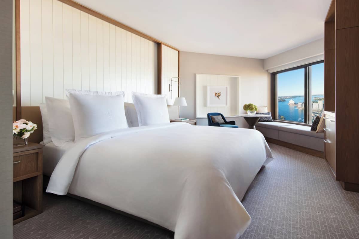 Quarto de hotel com uma cama grande, uma escrivaninha com cadeira, televisão e janela com vista para a água.