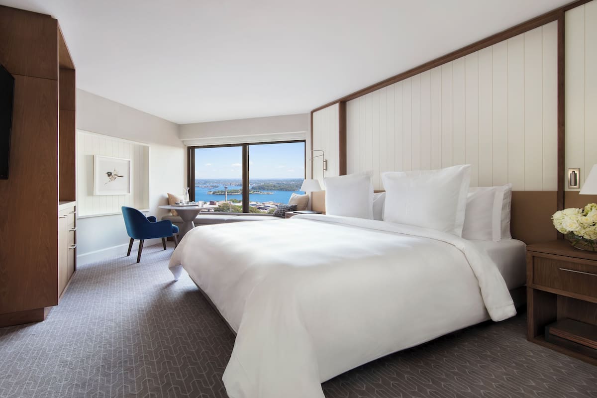 Quarto de hotel com cama grande, escrivaninha com cadeira, televisão e vista para a cidade.