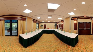 Uma sala de conferências com uma mesa comprida, cadeiras, tela de projetor e piso coberto de carpete.