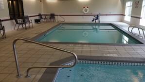 Piscina interna com piso ladrilhado, posto de salva-vidas e área de estar com cadeiras e mesas.