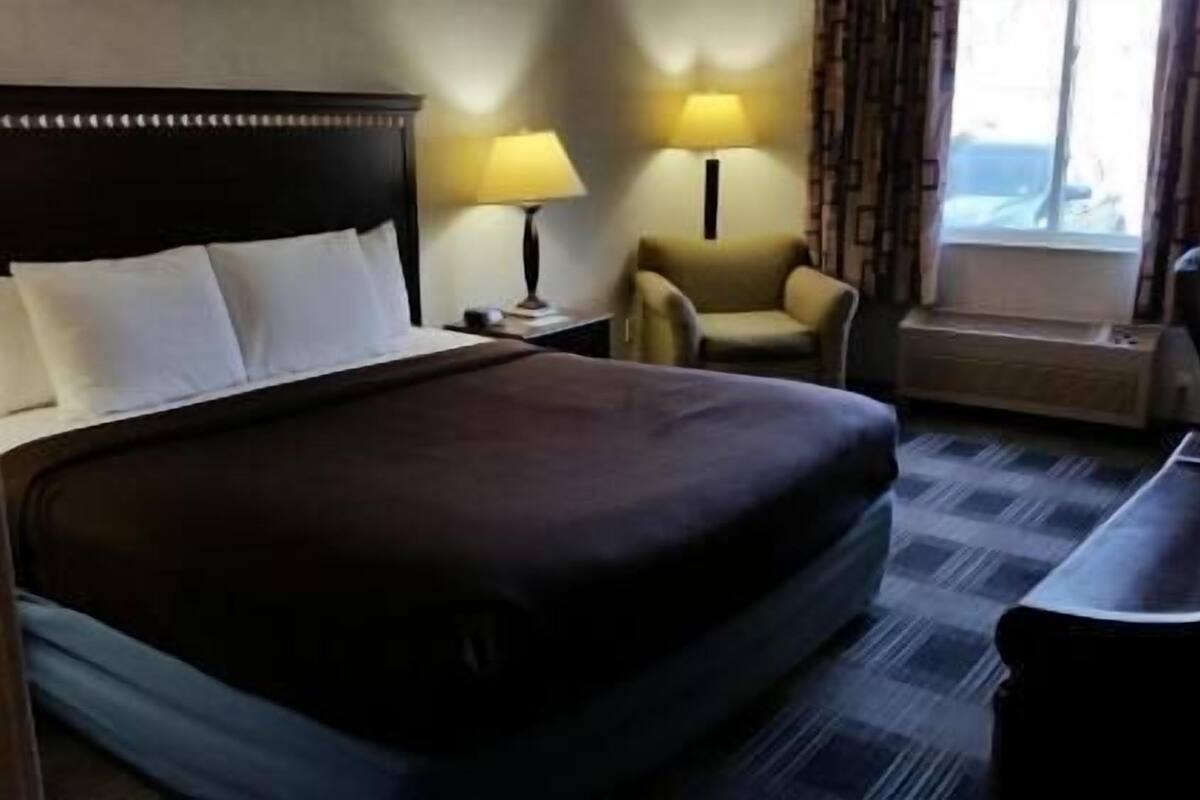 Quarto de hotel com cama, duas luminárias de cabeceira, uma cadeira e vista para o exterior.