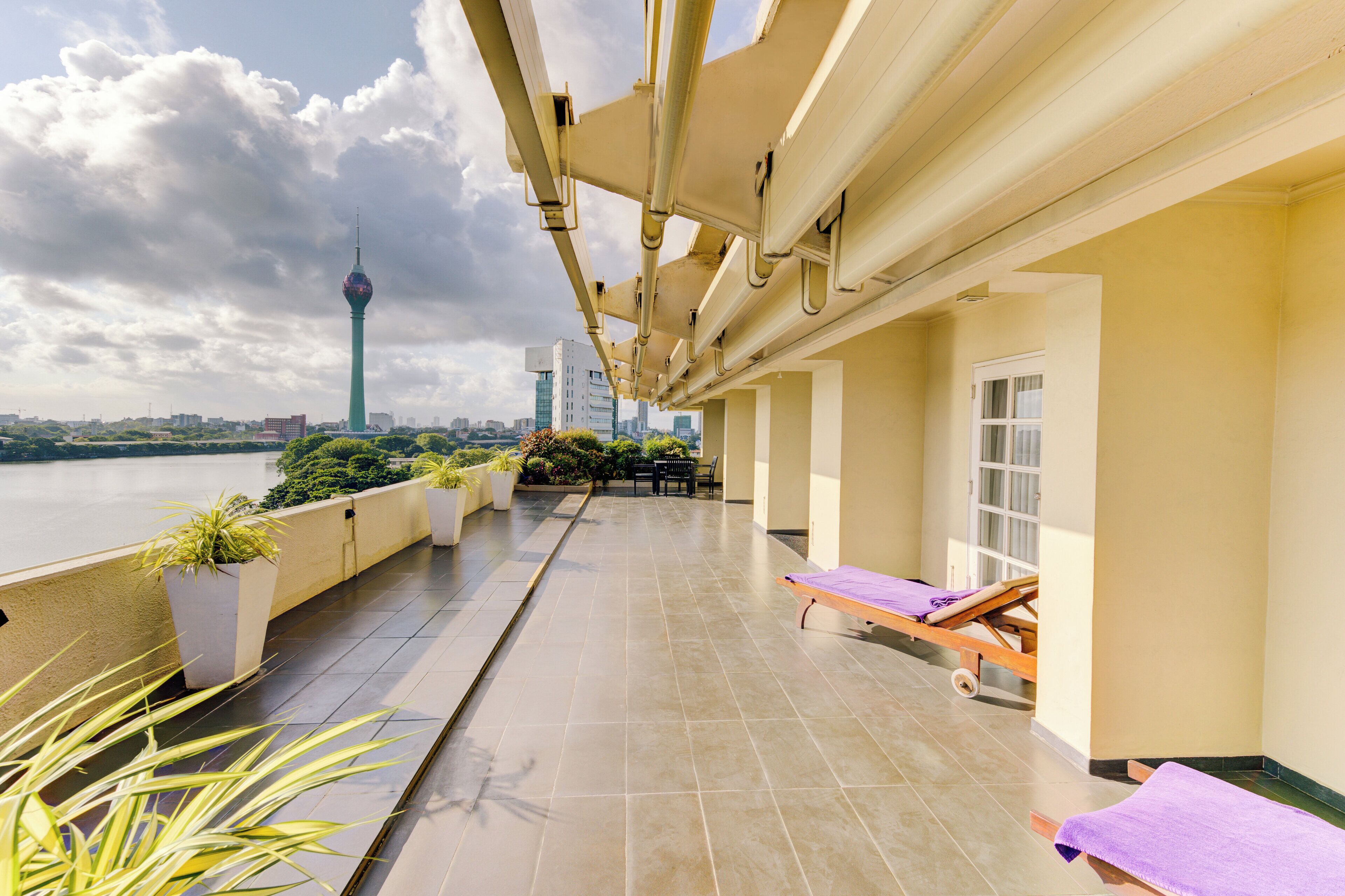 Terraço no telhado com vista para uma torre, plantas em vasos e cadeiras de descanso.