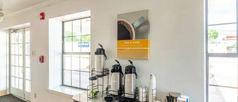 Uma área de recepção com um canto de café, uma obra de arte com uma xícara de café emoldurada e uma janela com vista para o exterior.