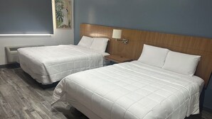 Duas camas de solteiro com cabeceiras de madeira, uma mesa de cabeceira, um abajur fixado na parede e uma ventilação.