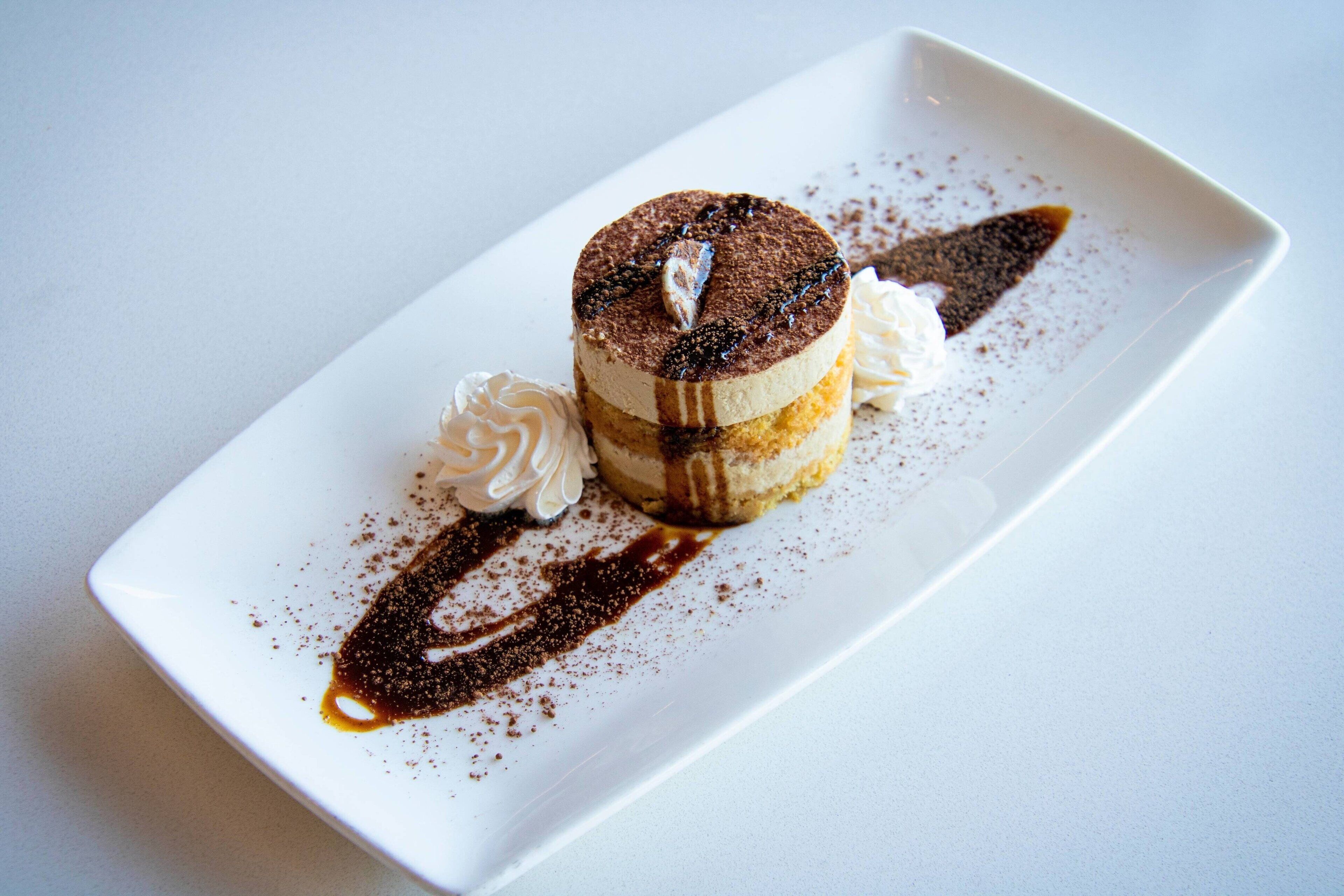 Sobremesa em um prato branco com chantilly e calda de chocolate.