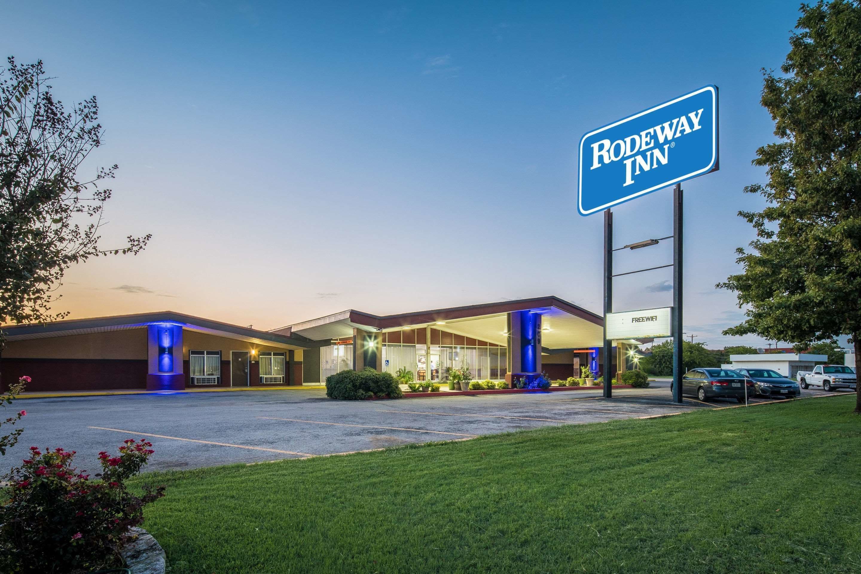 Um Rodeway Inn com uma placa grande, um estacionamento e um edifício com fachada de vidro.