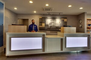 Bancada de recepção de hotel com um visor digital, um relógio e uma placa da Holiday Inn Express.