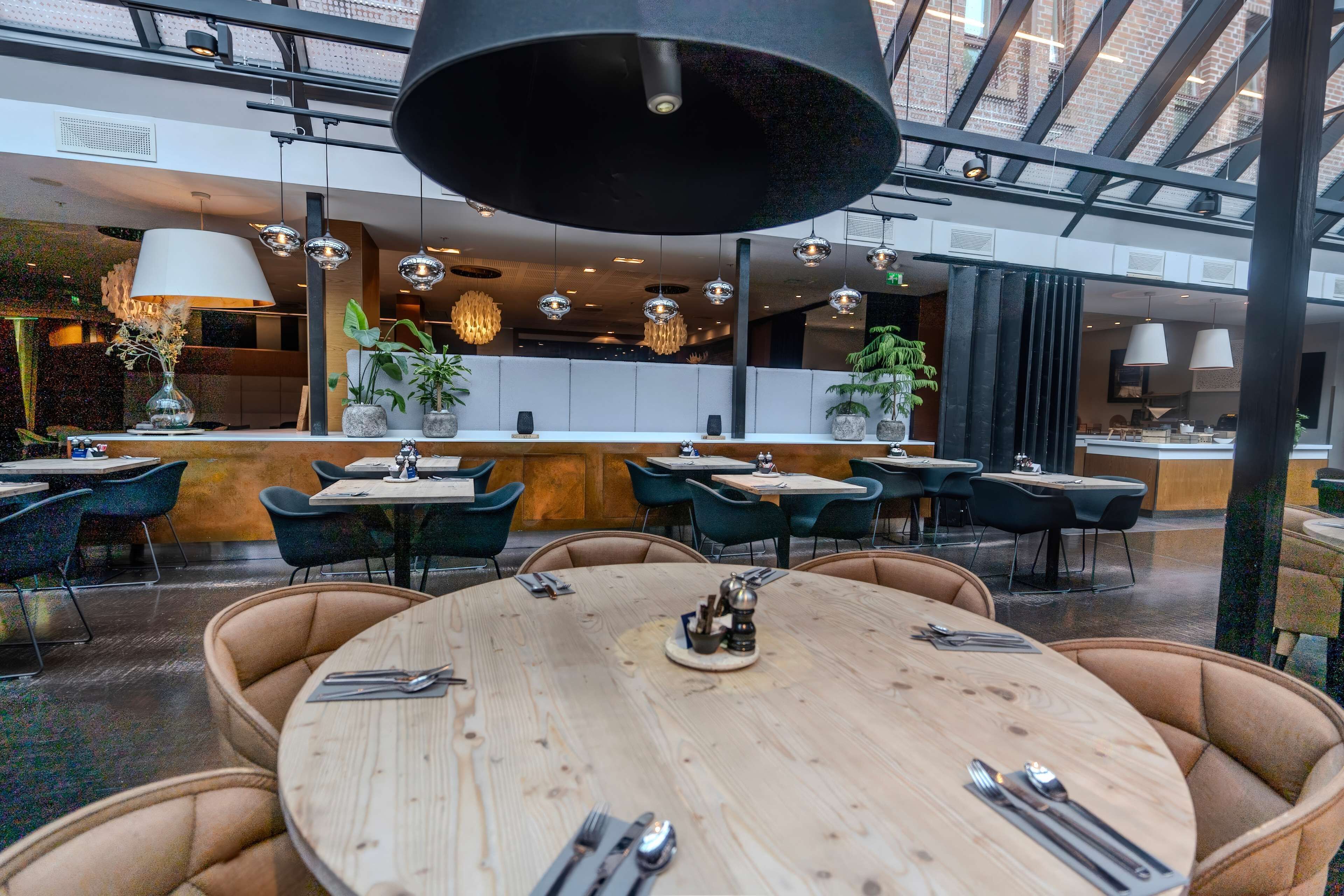 Restaurante moderno com mesas redondas, cadeiras pretas e iluminação pendente.