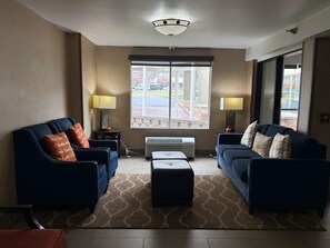 Quarto de hotel com duas sofás, uma mesa de centro, uma luminária e uma janela grande.