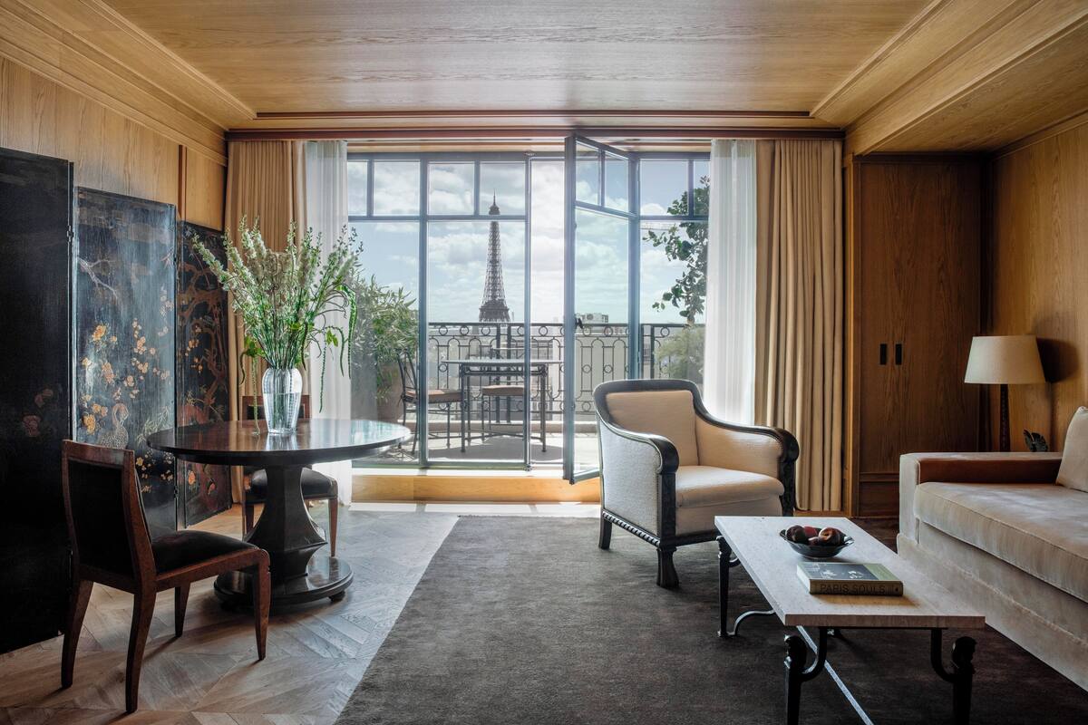 Quarto com teto de madeira, mesa de jantar com cadeiras, sofá, mesa de centro e vista da Torre Eiffel através de grandes janelas.