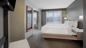 Quarto de hotel com uma cama grande, televisão na parede, escrivaninha e janela com cortinas.