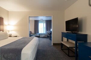 Quarto de hotel com uma cama grande, uma escrivaninha com cadeira, televisão e vista para o corredor.