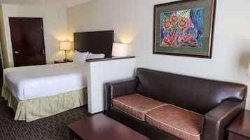 Quarto de hotel com cama, sofá, mesa e um quadro na parede.