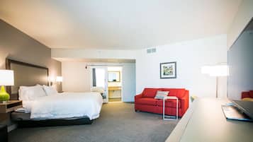 Quarto de hotel com uma cama, um sofá vermelho, uma escrivaninha e uma televisão.