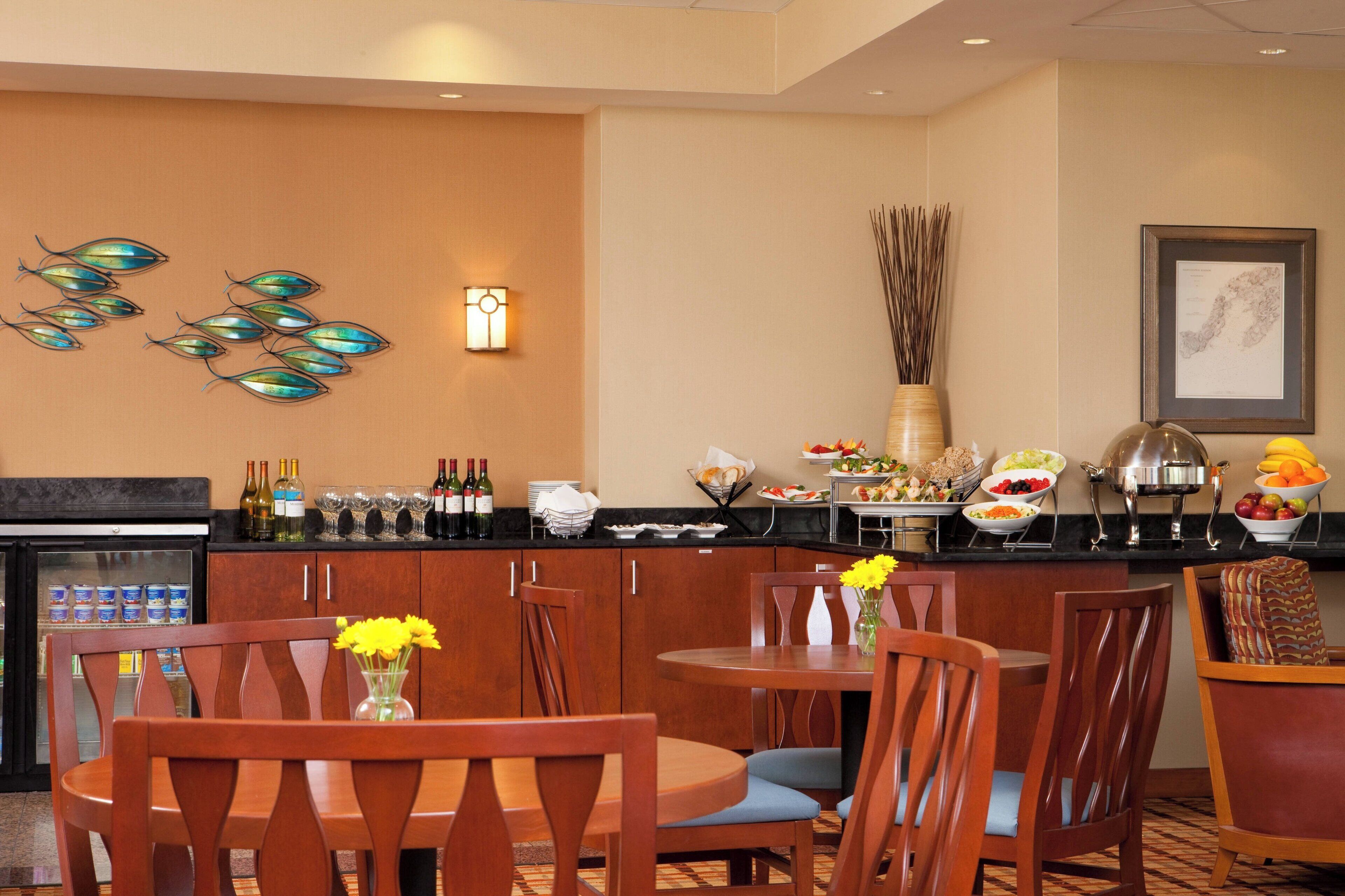Uma área de bar de hotel com cadeiras de madeira, um buffet com diversos alimentos e uma parede decorativa com luzes em formato de folhas.