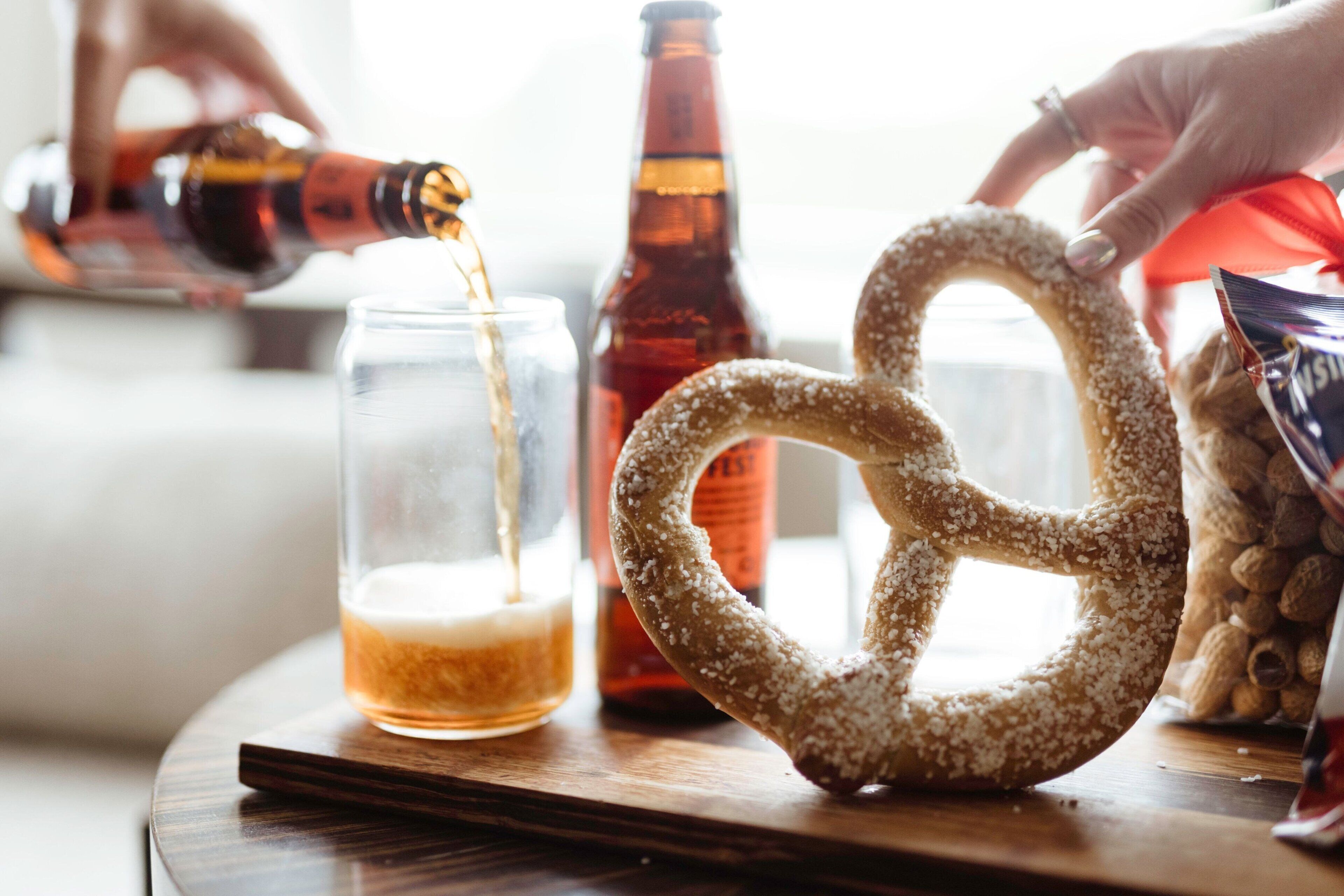 Um pretzel em formato de coração sobre uma mesa de madeira com uma garrafa de cerveja e cerveja sendo servida em um copo.