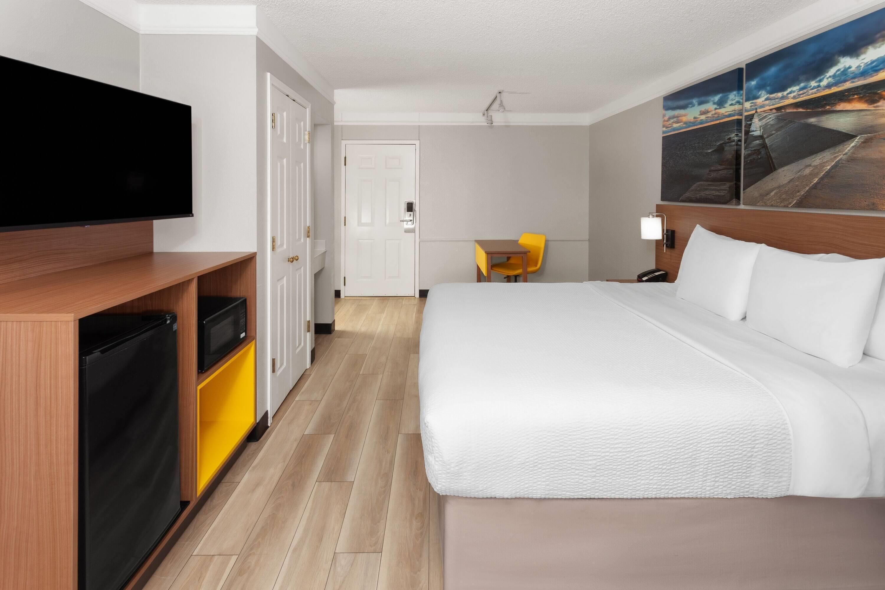 Quarto de hotel com uma cama grande, televisão de tela plana, escrivaninha com cadeira e um quadro na parede.