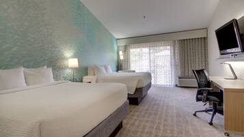Quarto de hotel com duas camas, uma escrivaninha com cadeira, televisão e janela com cortinas.
