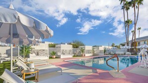 Uma área à beira da piscina com espreguiçadeiras, guarda-sóis e uma piscina.