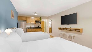 Quarto de hotel moderno com cozinha compacta, televisão de tela plana e uma cama grande.