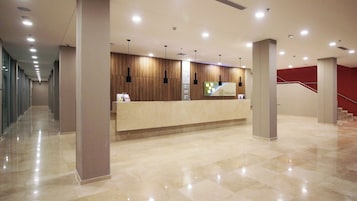 Uma área de recepção moderna com piso de mármore, painéis de madeira e um balcão de atendimento.