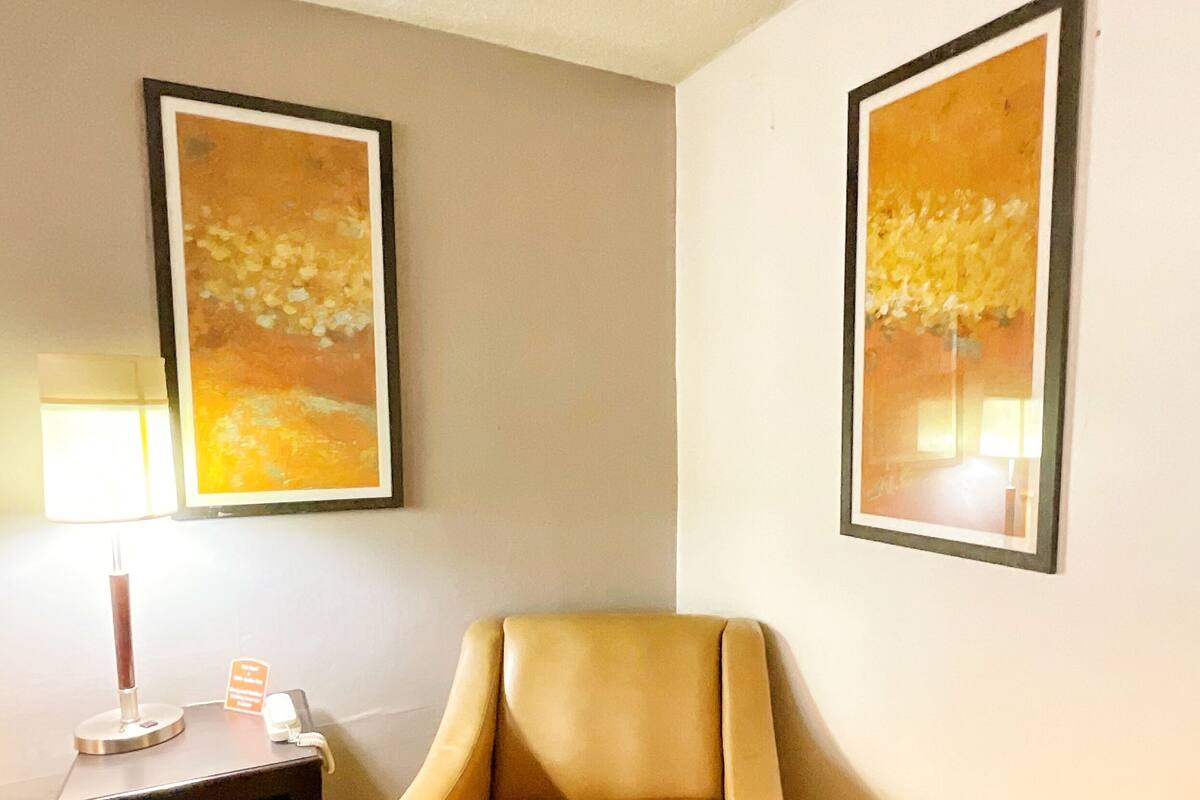 Quarto nos fundos com uma poltrona bege, uma mesinha com abajur e duas pinturas abstratas emolduradas nas paredes.