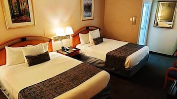 Quarto de hotel com duas camas, mesa de cabeceira com luminárias e quadros nas paredes.
