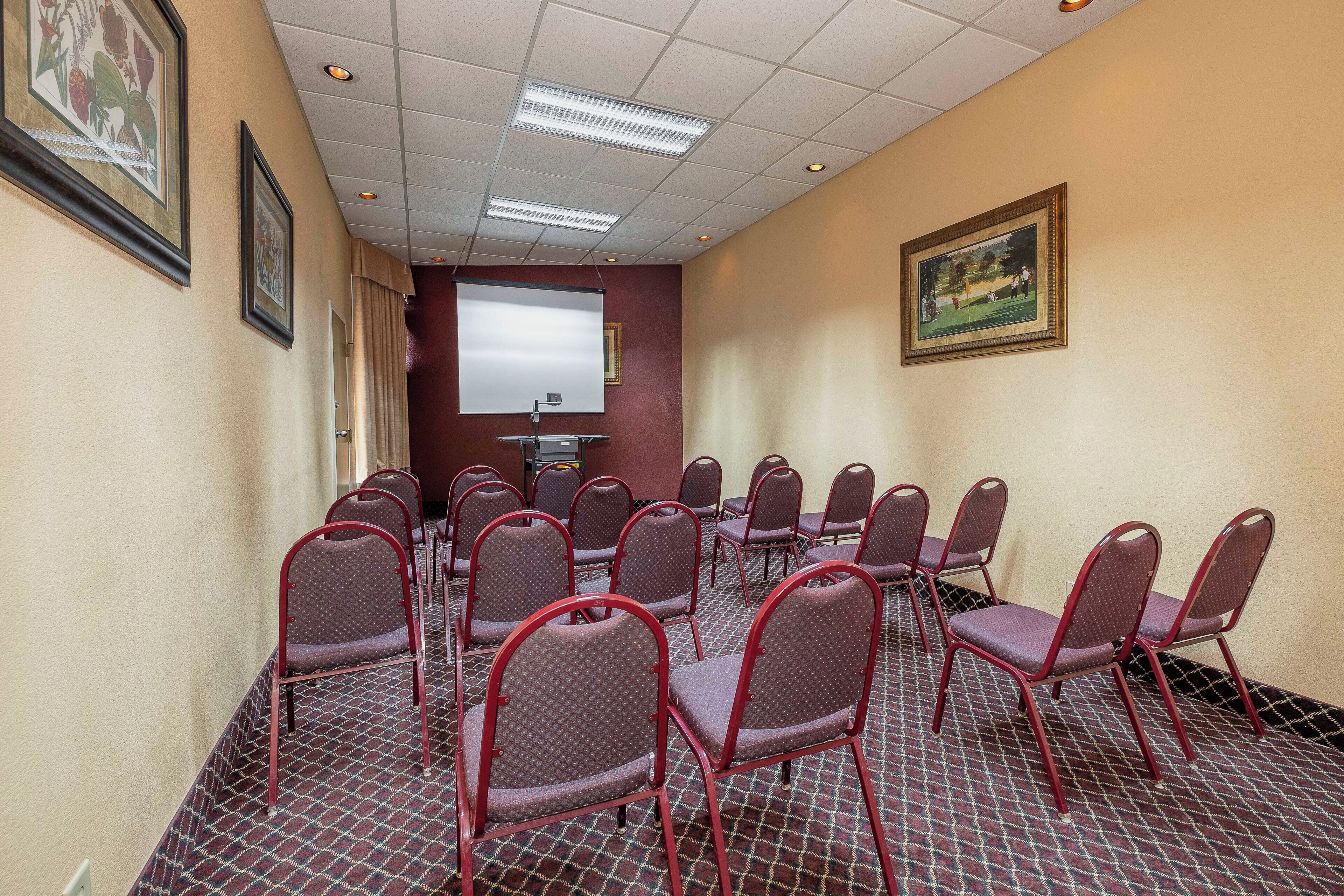 Uma sala de conferência com fileiras de cadeiras, uma tela de projetor e piso coberto de carpete.