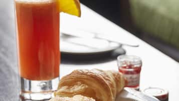 Um croissant num prato com uma faca e um copo de sumo de laranja com uma fatia de limão.