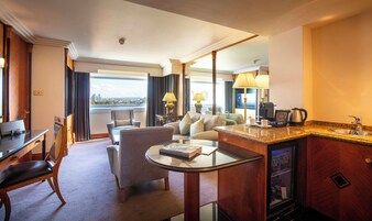 Quarto de hotel com área de estar, mesa de jantar, cozinha e vista para a cidade.