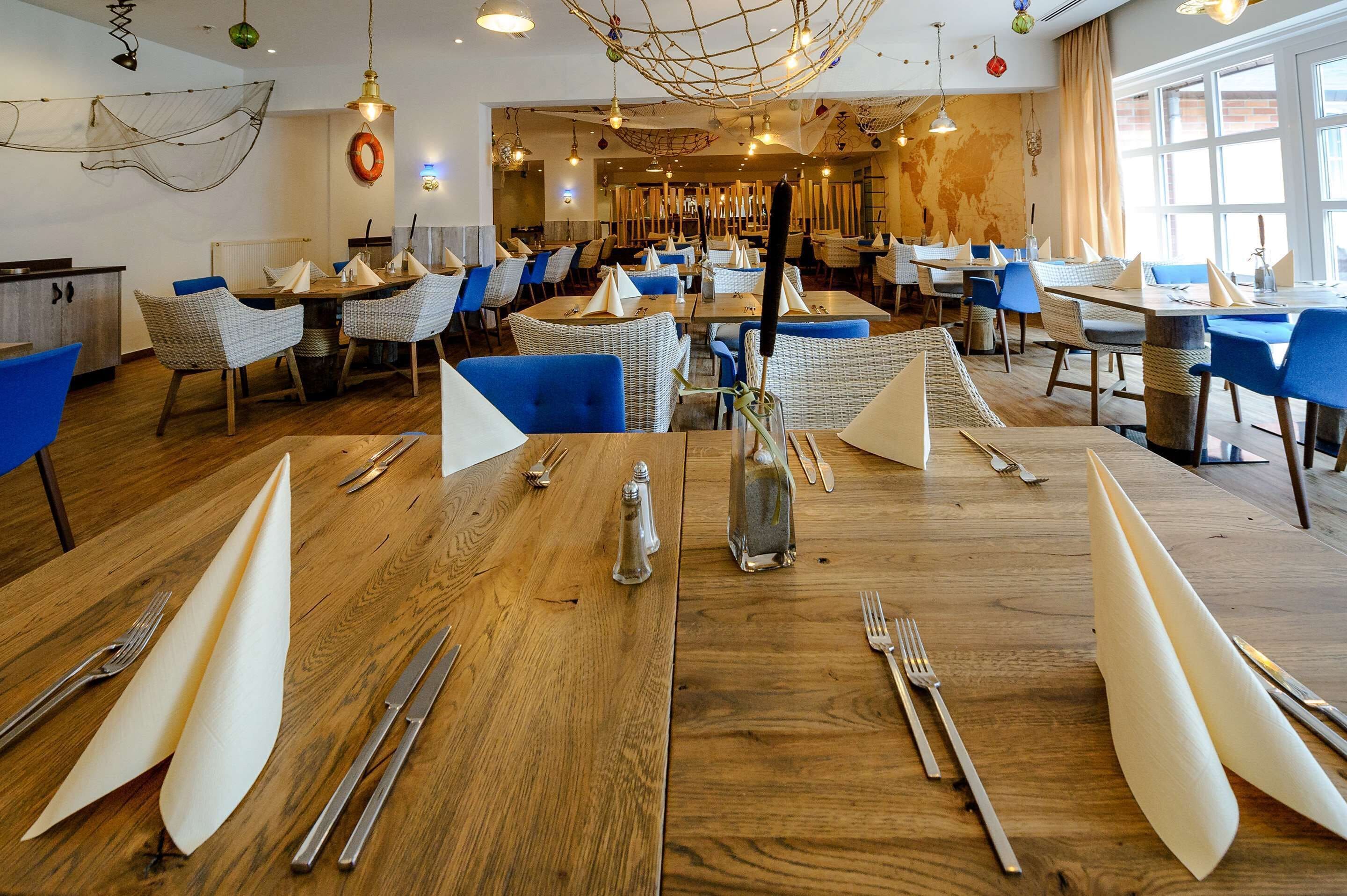 Um restaurante com mesas de madeira, cadeiras azuis e luminárias pendentes.