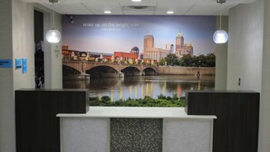 Uma área de recepção com um mural da paisagem urbana, um balcão de atendimento e um elemento de água.