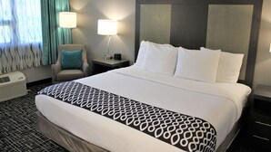 Quarto de hotel com uma cama grande, uma cadeira, mesa de cabeceira com abajur e janela com cortinas.