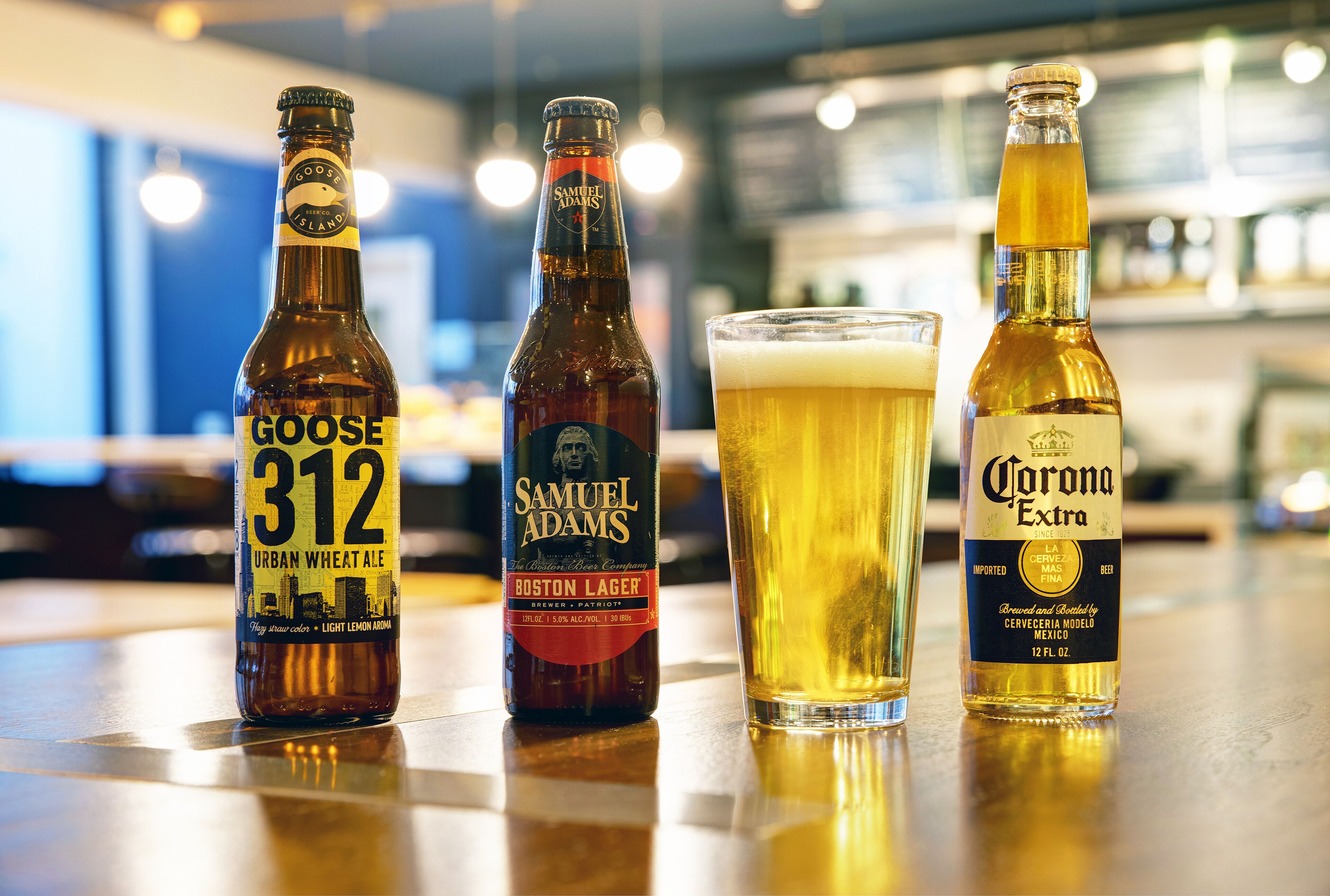 Três garrafas de cerveja e um copo de cerveja em um balcão de bar.