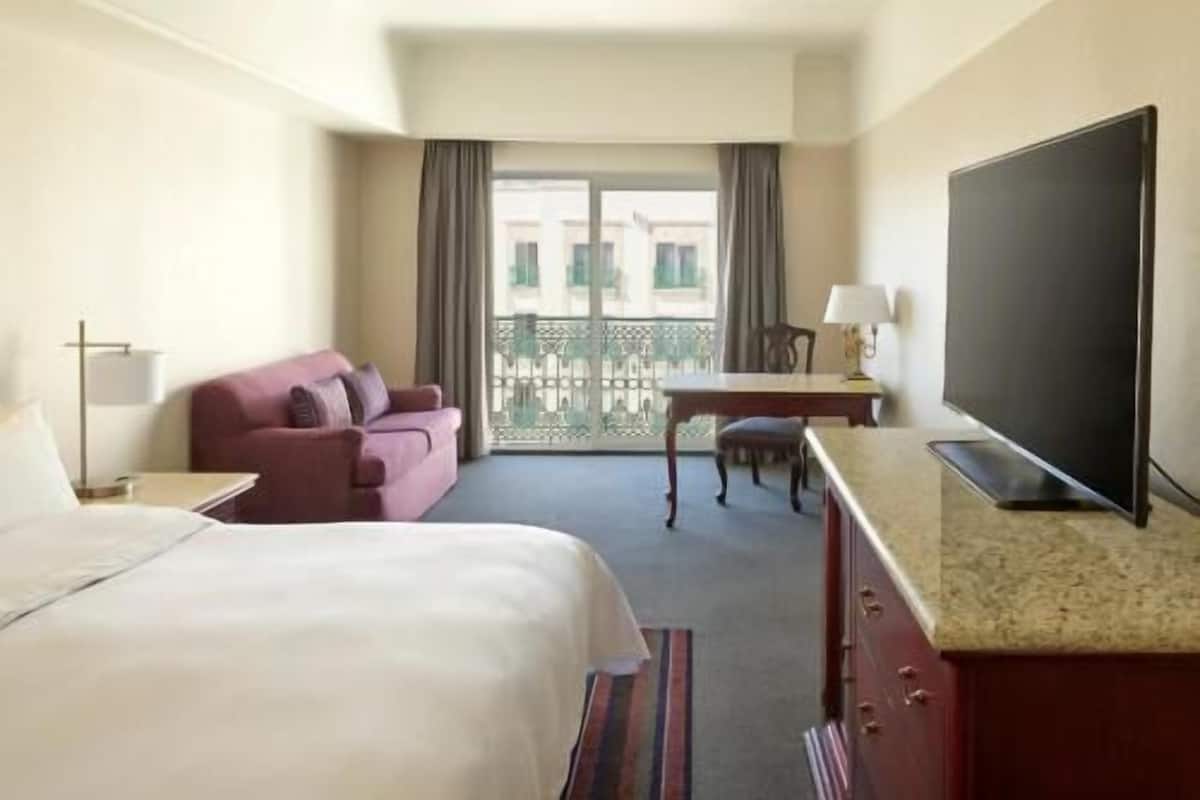 Quarto de hotel com cama, sofá, televisão e varanda com vista.