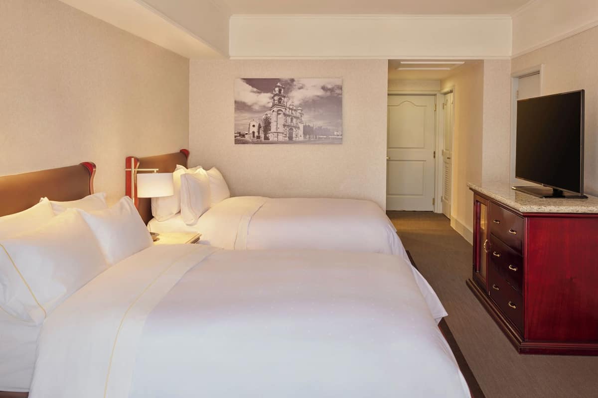Quarto de hotel com duas camas, uma TV de tela plana, um quadro na parede e uma porta para o banheiro.