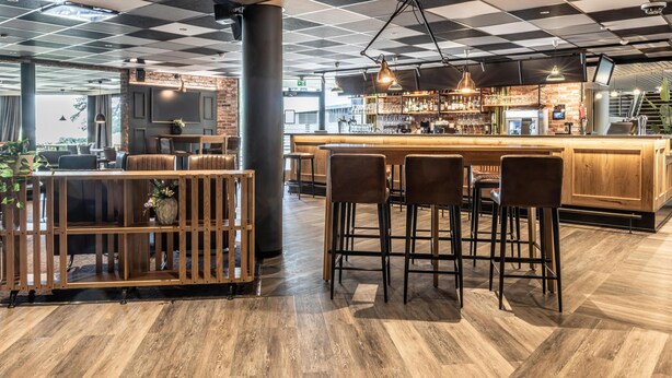 Uma área de bar com mobiliário de madeira, teto quadriculado e balcão.
