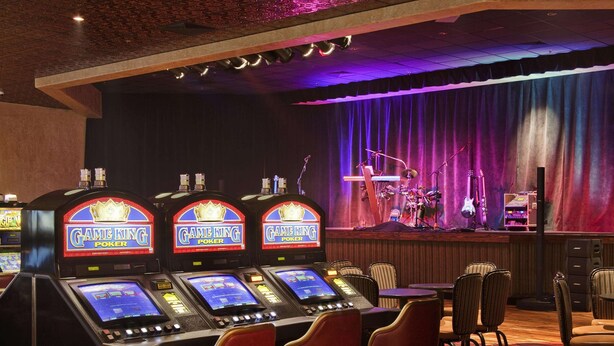Um cassino com várias máquinas de 'Game King Poker', um palco com equipamentos musicais e uma área de bar.