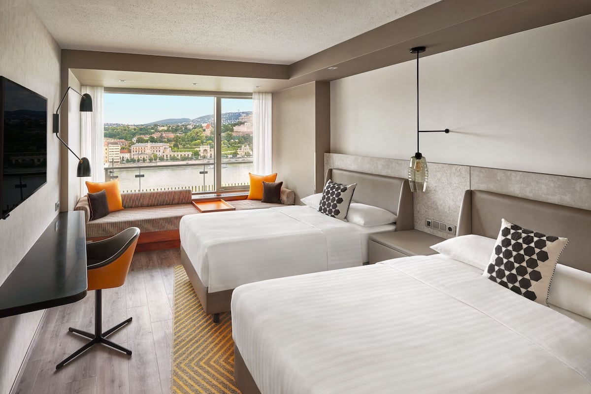 Quarto de hotel com duas camas, um sofá, uma escrivaninha e uma televisão.