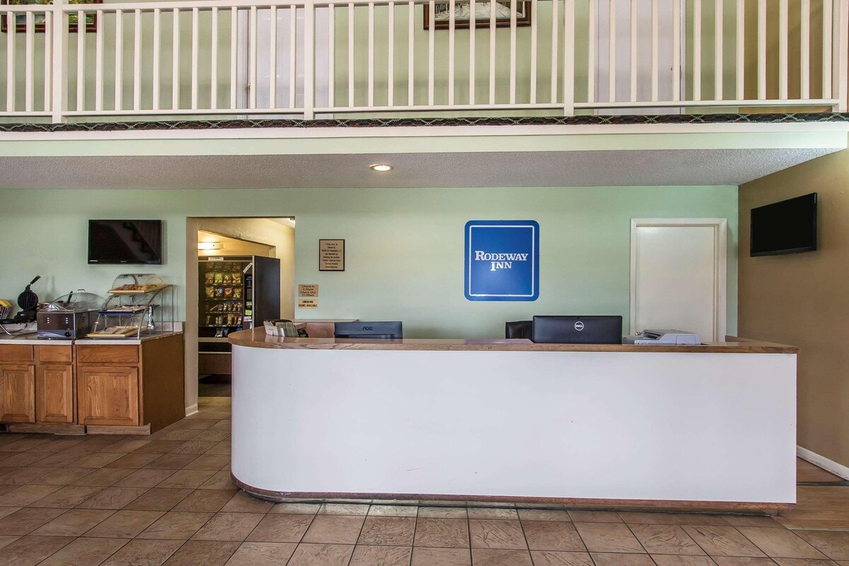 Uma área de recepção de hotel com balcão de check-in, máquina de venda automática e placa da Rodeway Inn.