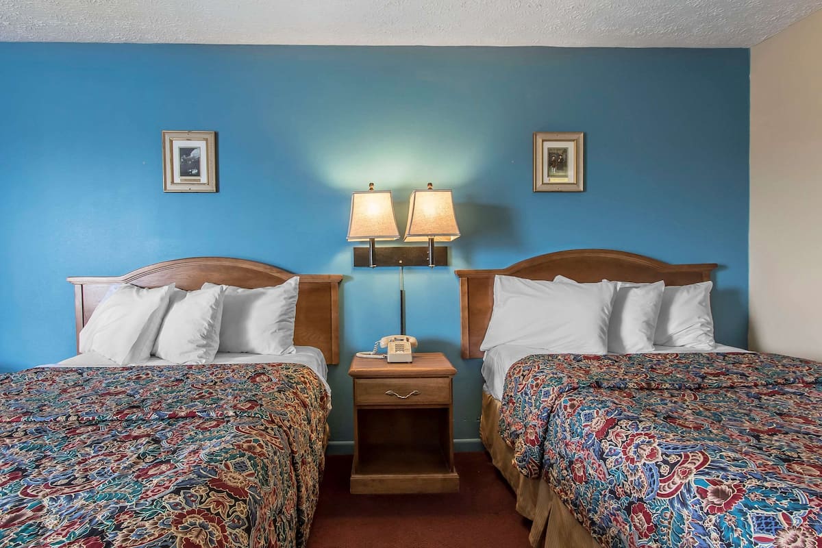 Quarto de hotel com duas camas, cada uma com colcha estampada, mesa de cabeceira com abajur e quadros nas paredes.