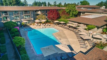 Um hotel com uma piscina grande, área de estar externa com guarda-sóis e um jardim paisagístico.